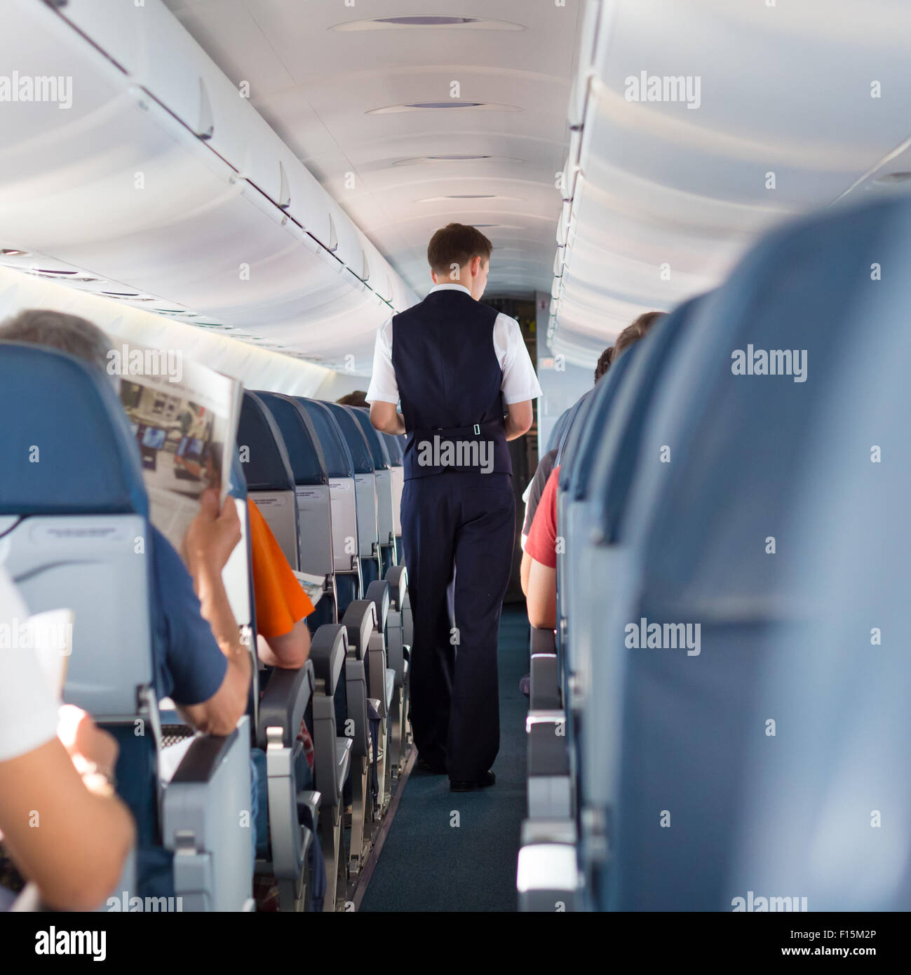 Interior of airplane with passengers on seats and steward walking the ...