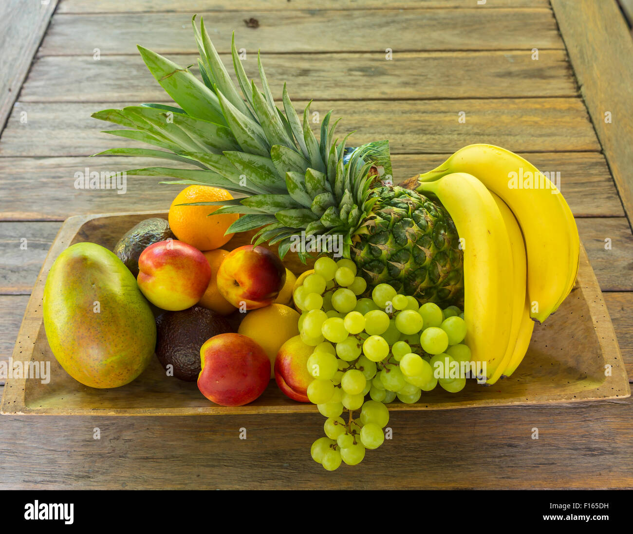 Wooden bowl full of fruit, bananas, pineapple, grapes, mango ...
