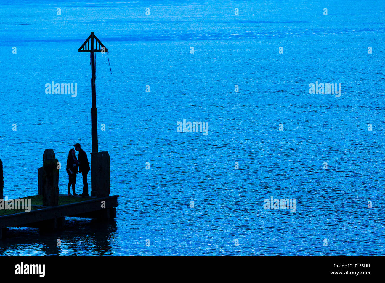 Romance: A young couple in silhouette about to kiss standing on a jetty ...