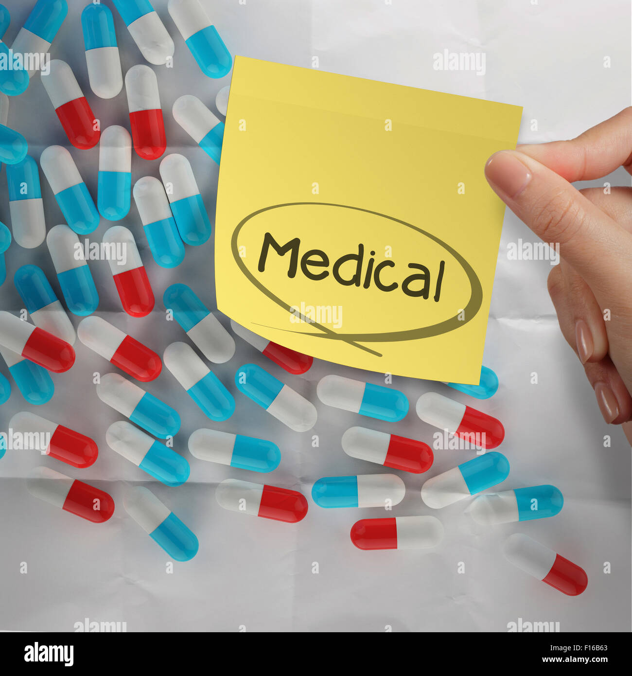 hand holding sticky note medical with Pills spilling on crumpled paper ...