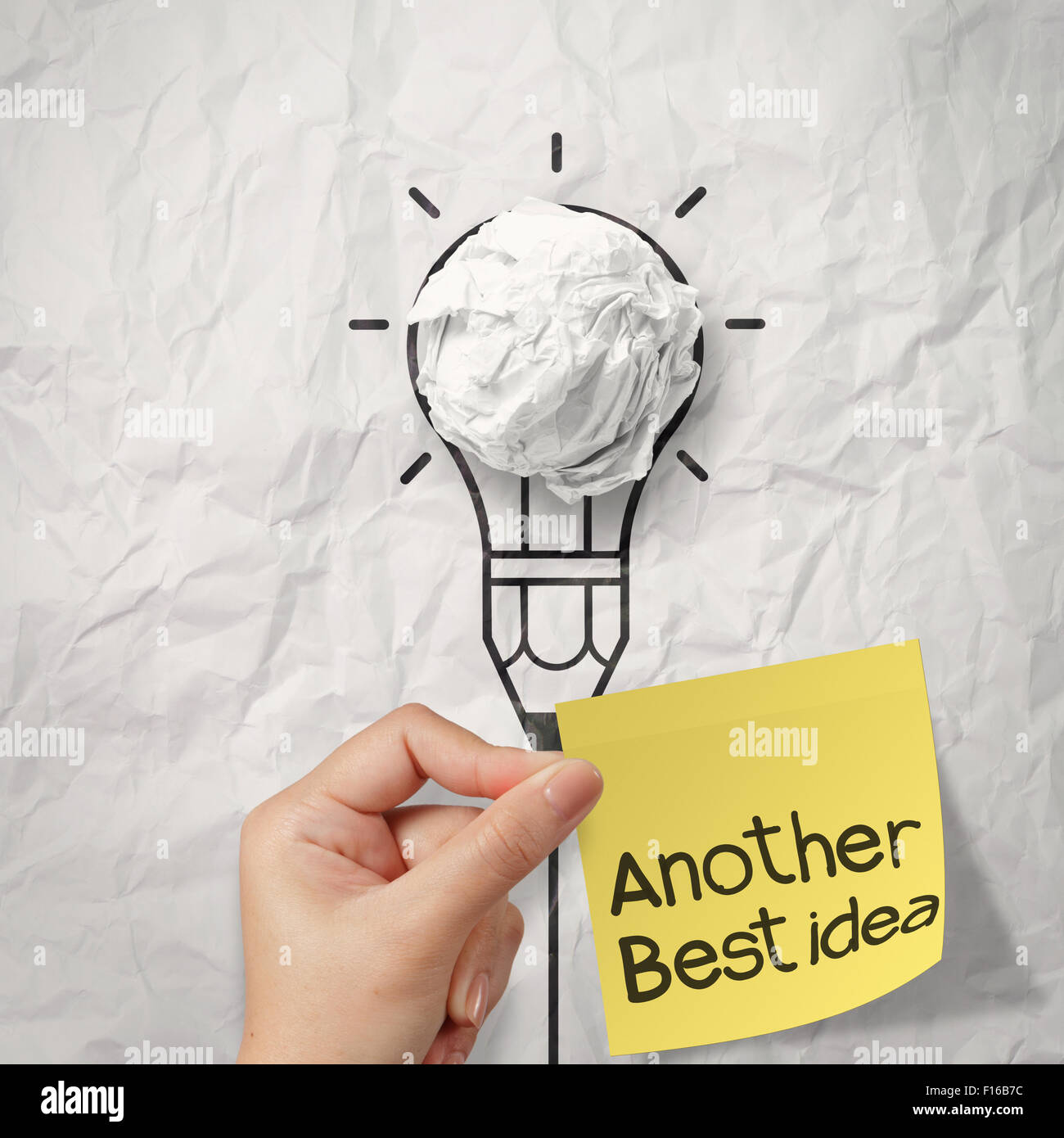 hand holding sticky note with another idea light bulb on crumpled paper ...