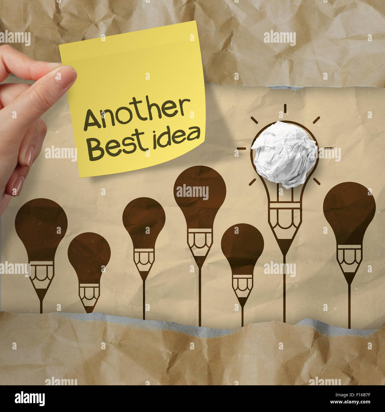 hand holding sticky note with another idea light bulb on crumpled paper ...