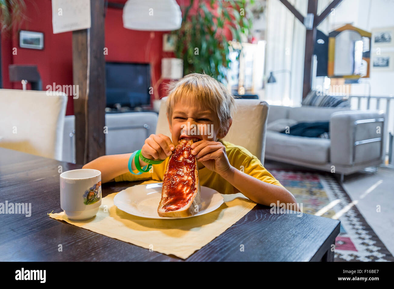 blond boy in yellow jersey eating at the table bread and jam Stock ...