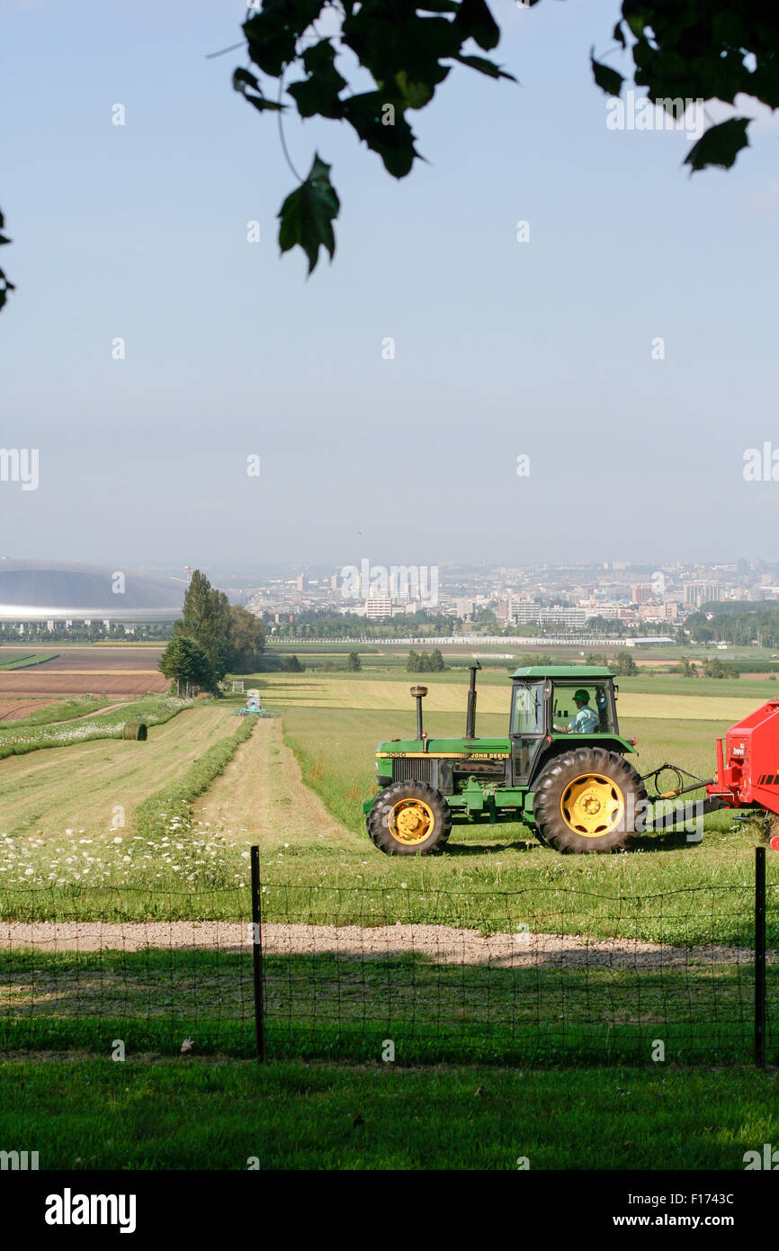 Tractor profile on grass field with big sky and city in far distance ...