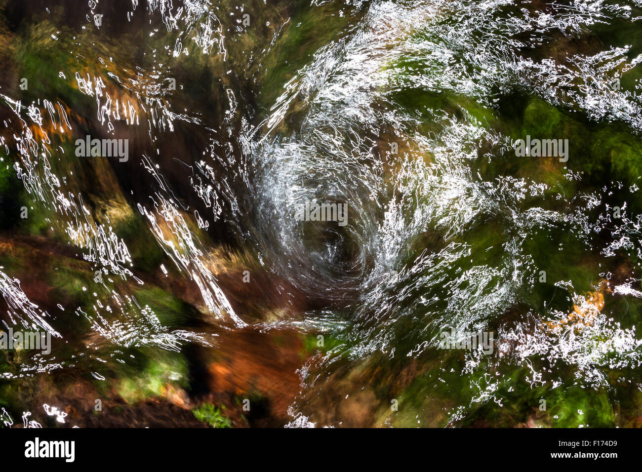 close up of a whirlpool on a small river with green and orange leaves ...