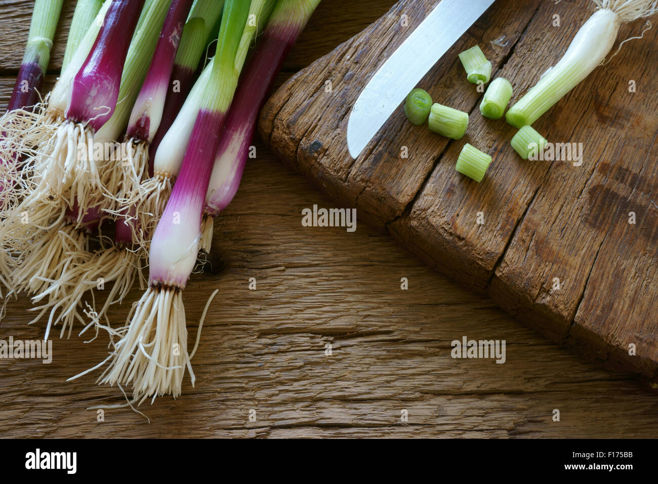 Fresh red spring onions and a kitchen knife on an old wooden cutting ...