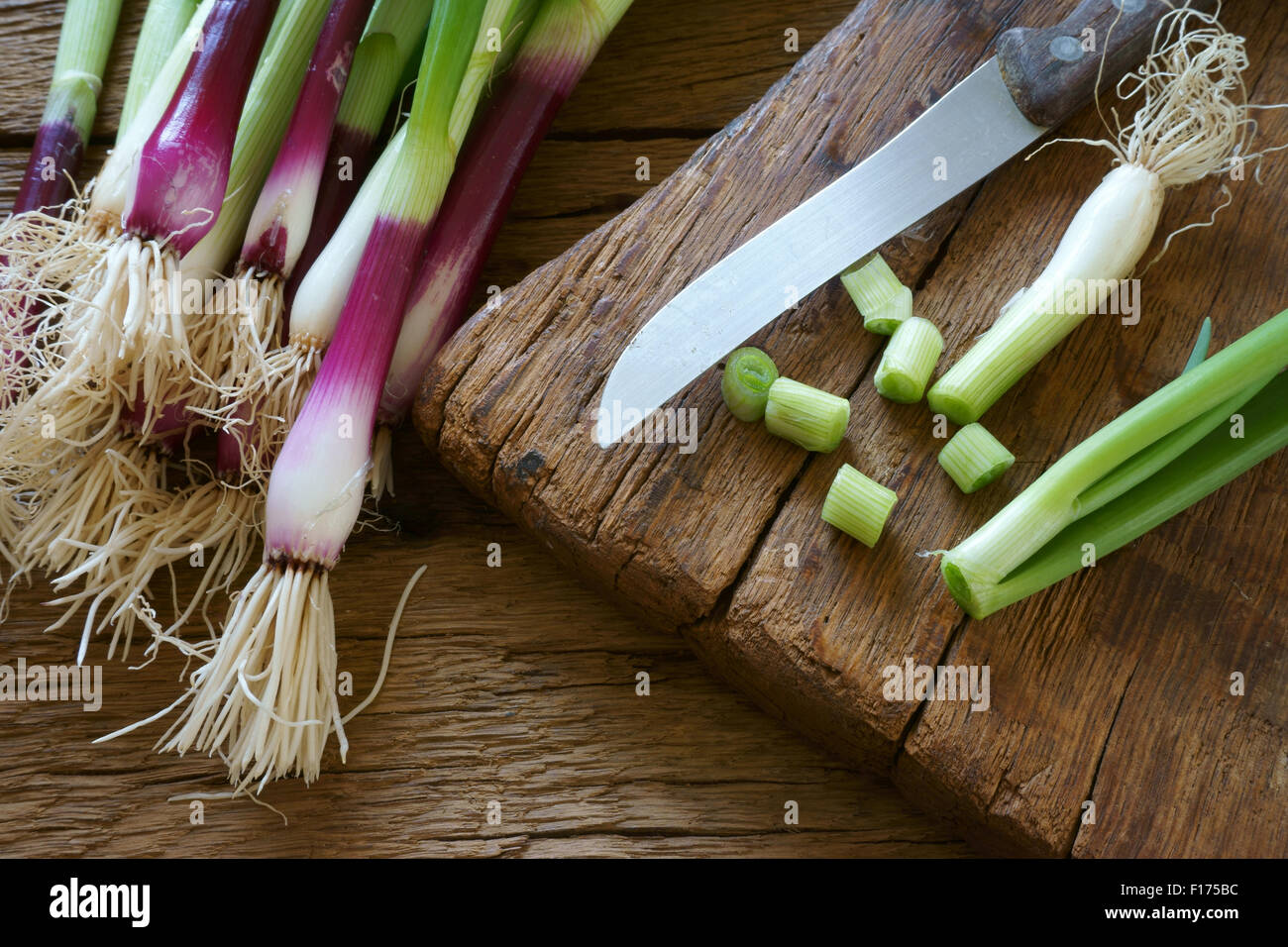 Fresh red spring onions and a kitchen knife on an old wooden cutting ...