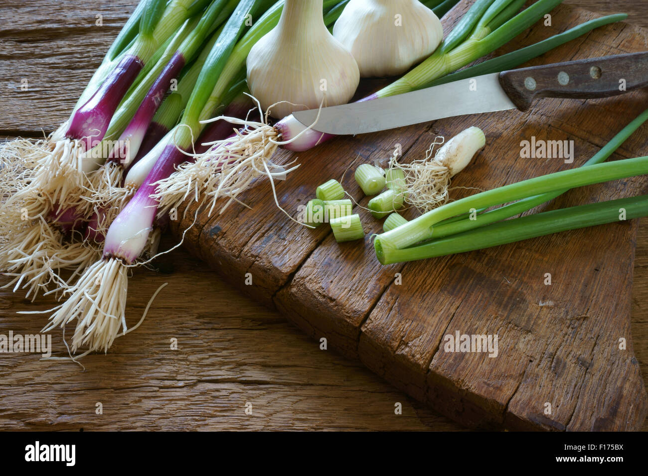 Fresh red spring onions, garlic bulb and a kitchen knife on an old ...
