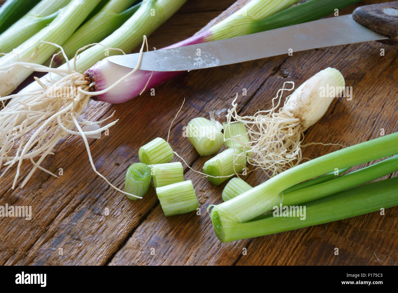 Cut spring onions with a kitchen knife on a rustic wooden cutting board ...