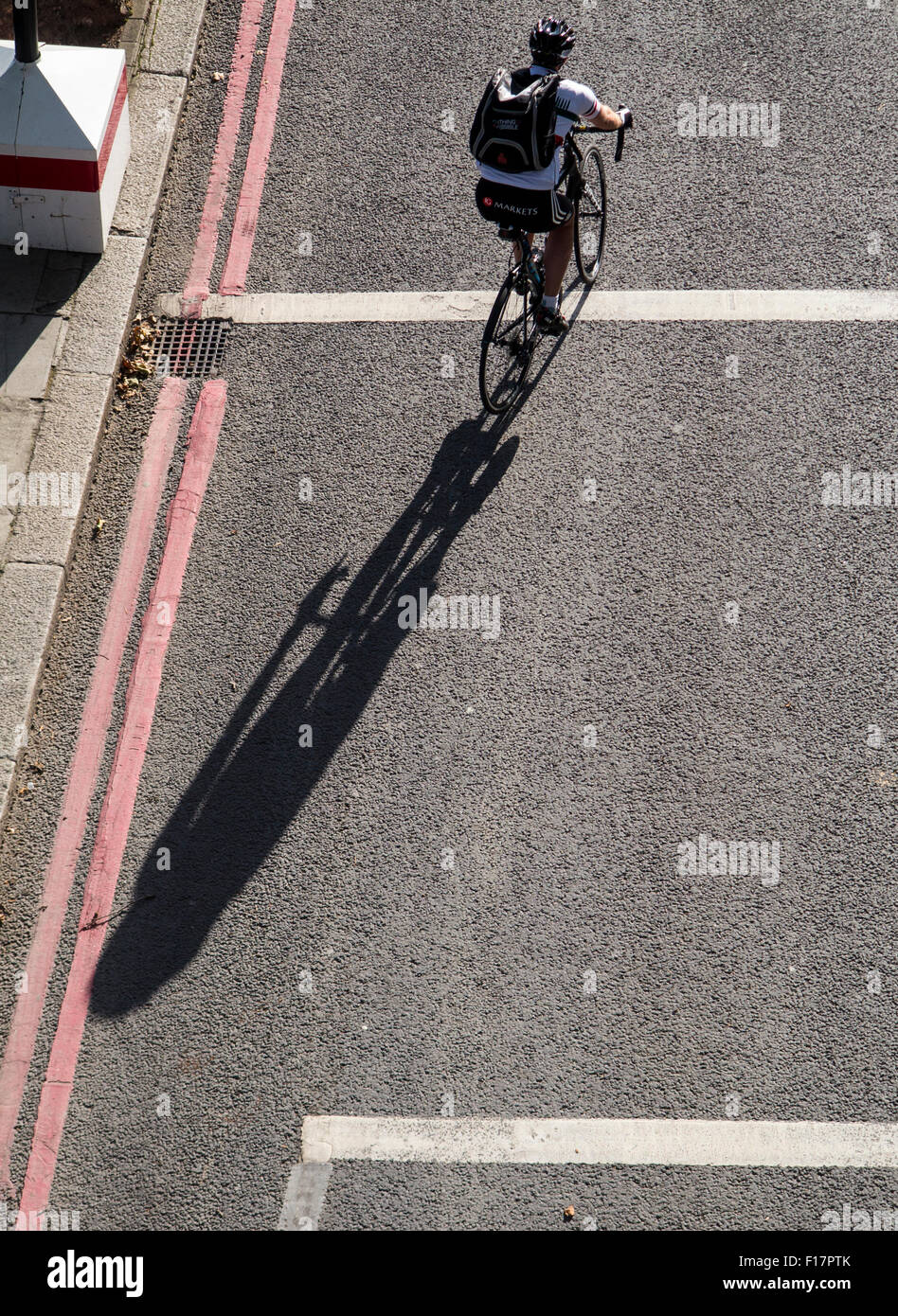 A cyclist at the traffic lights in afternoon sunlight on a busy high ...