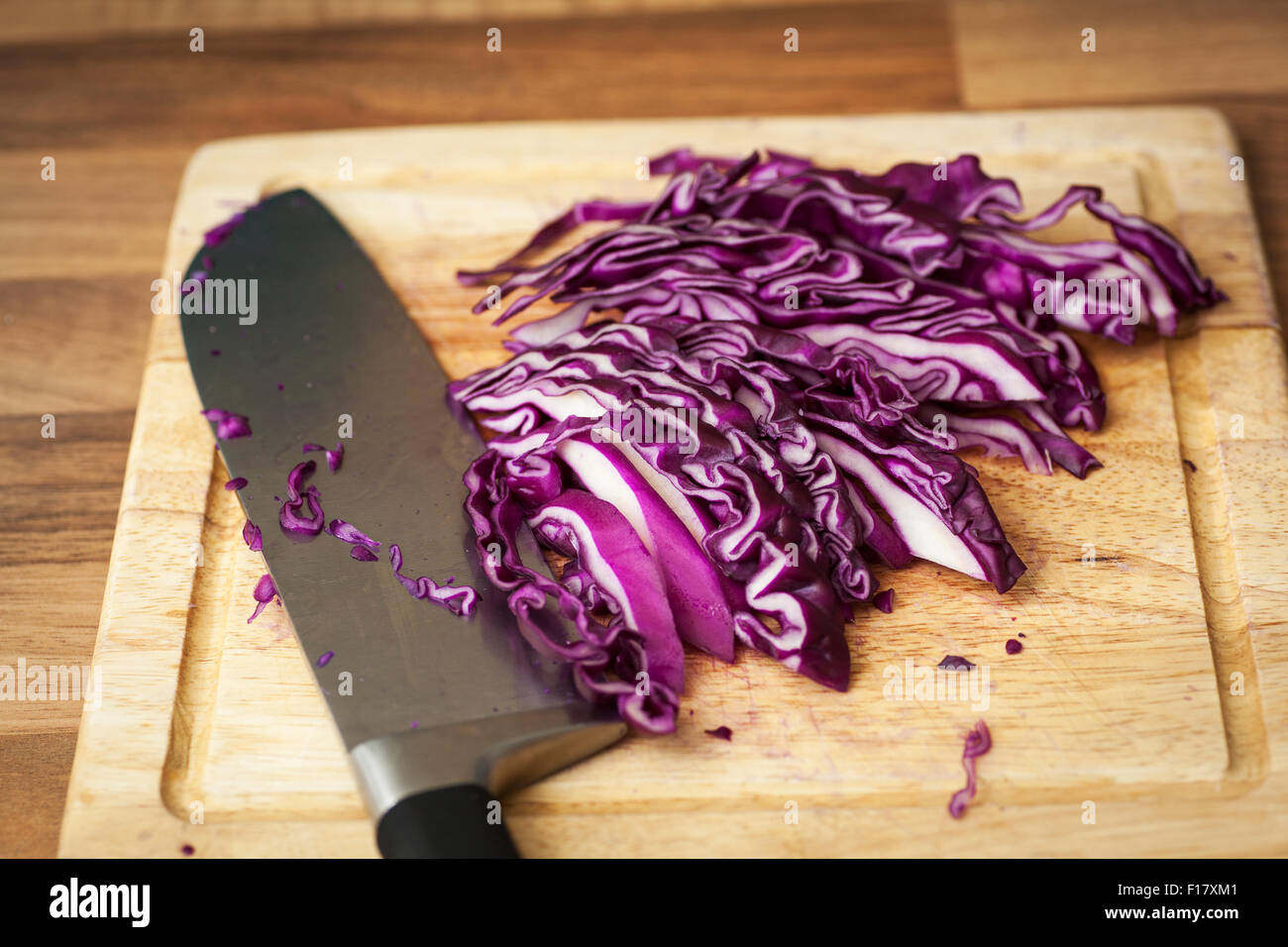 Sliced fresh red cabbage on a small wooden chopping board and cooks ...