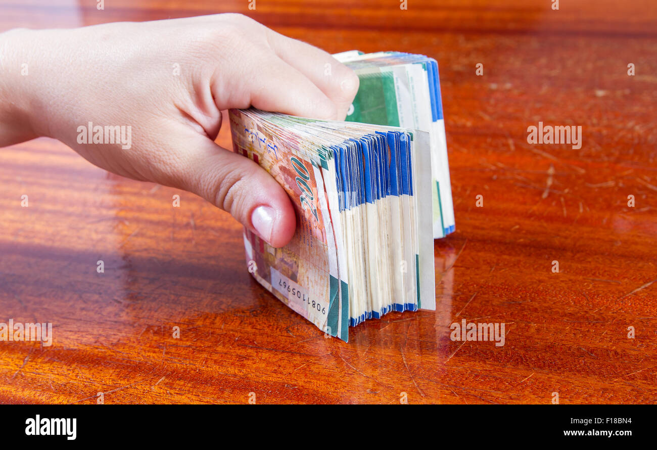 A female hand holding two hundred shekel bank notes against wood ...