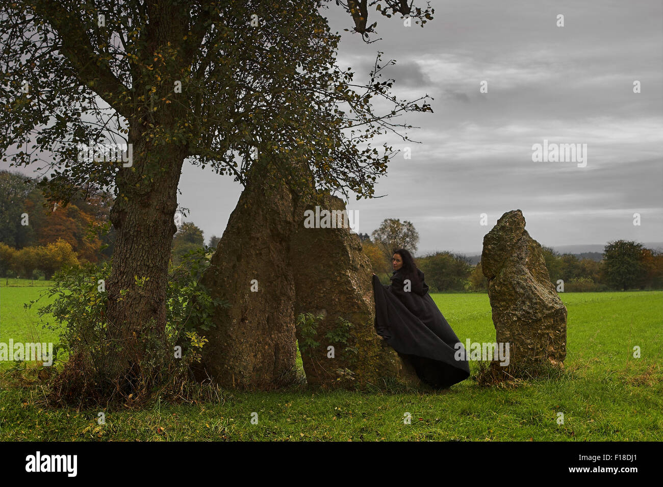 Woman or witch in black cape walking around a group of menhirs and a ...