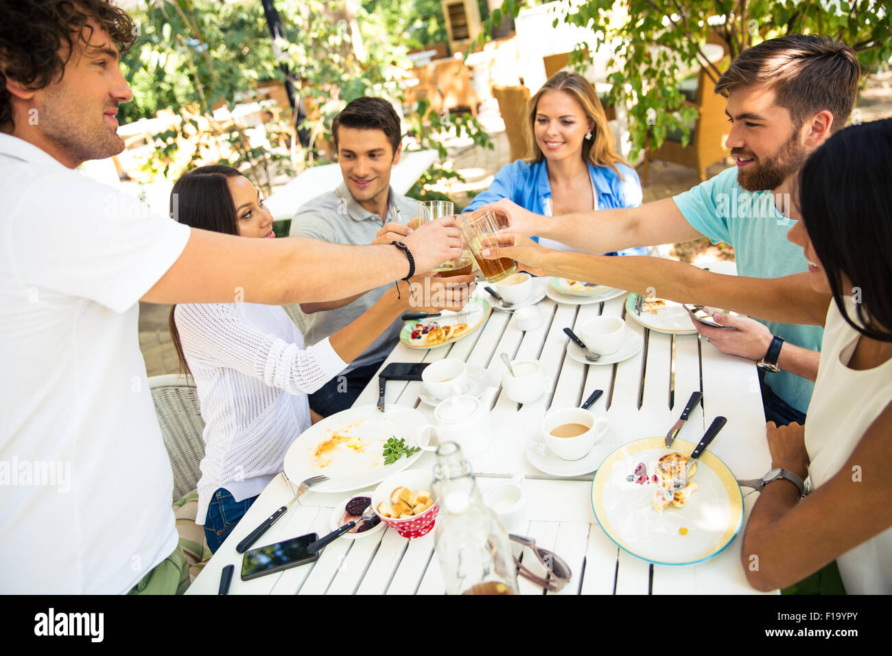 Group of a young friends making toast around table at dinner party in ...