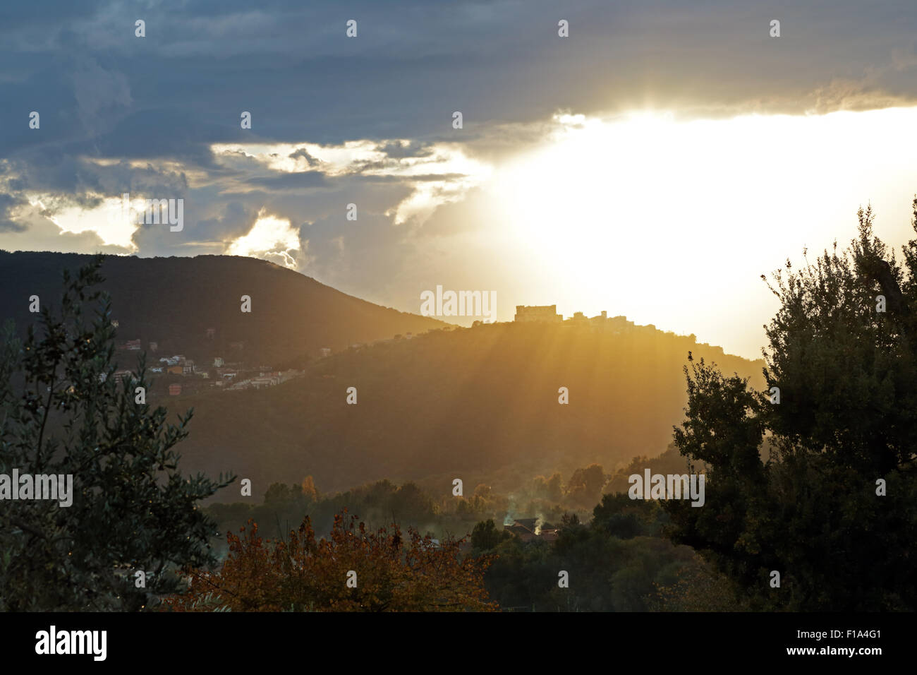 Sun rays through the clouds light up a small town on a hill in the ...