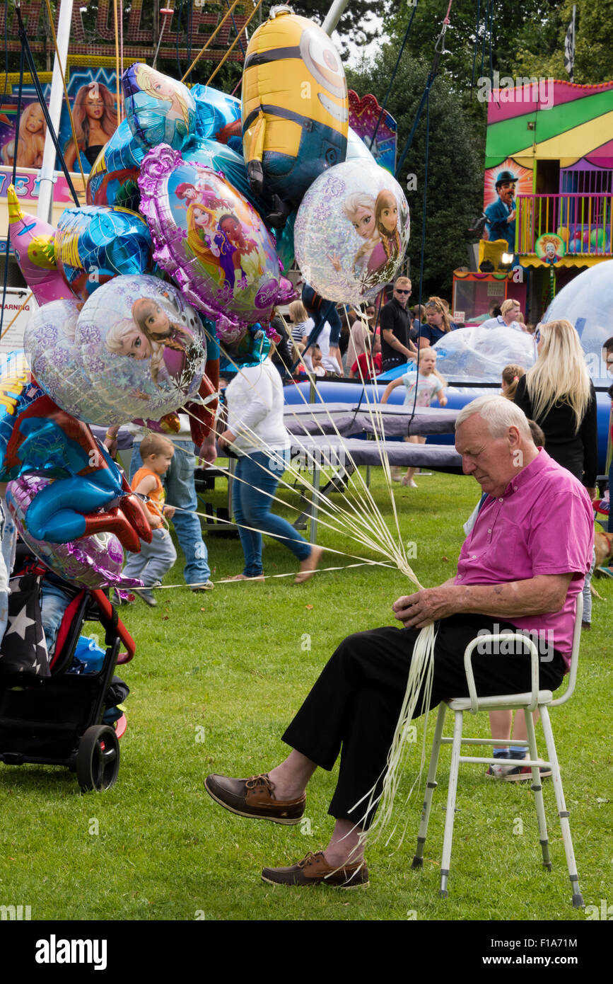 An old man sat in chair holding balloons falling to sleep at the fun ...