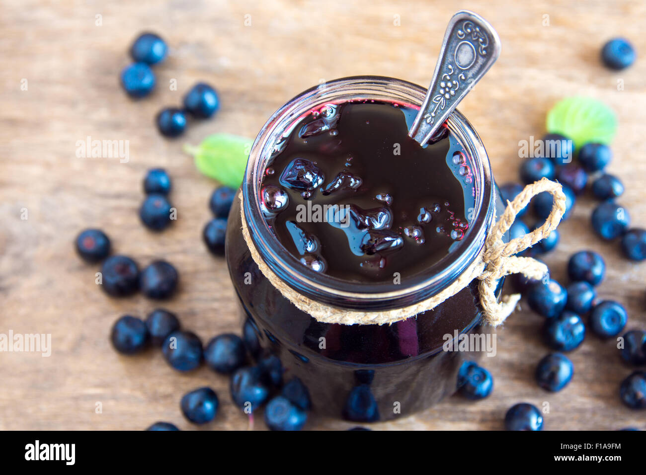Blueberry jam in jar with berries and leaves over rustic wooden table ...