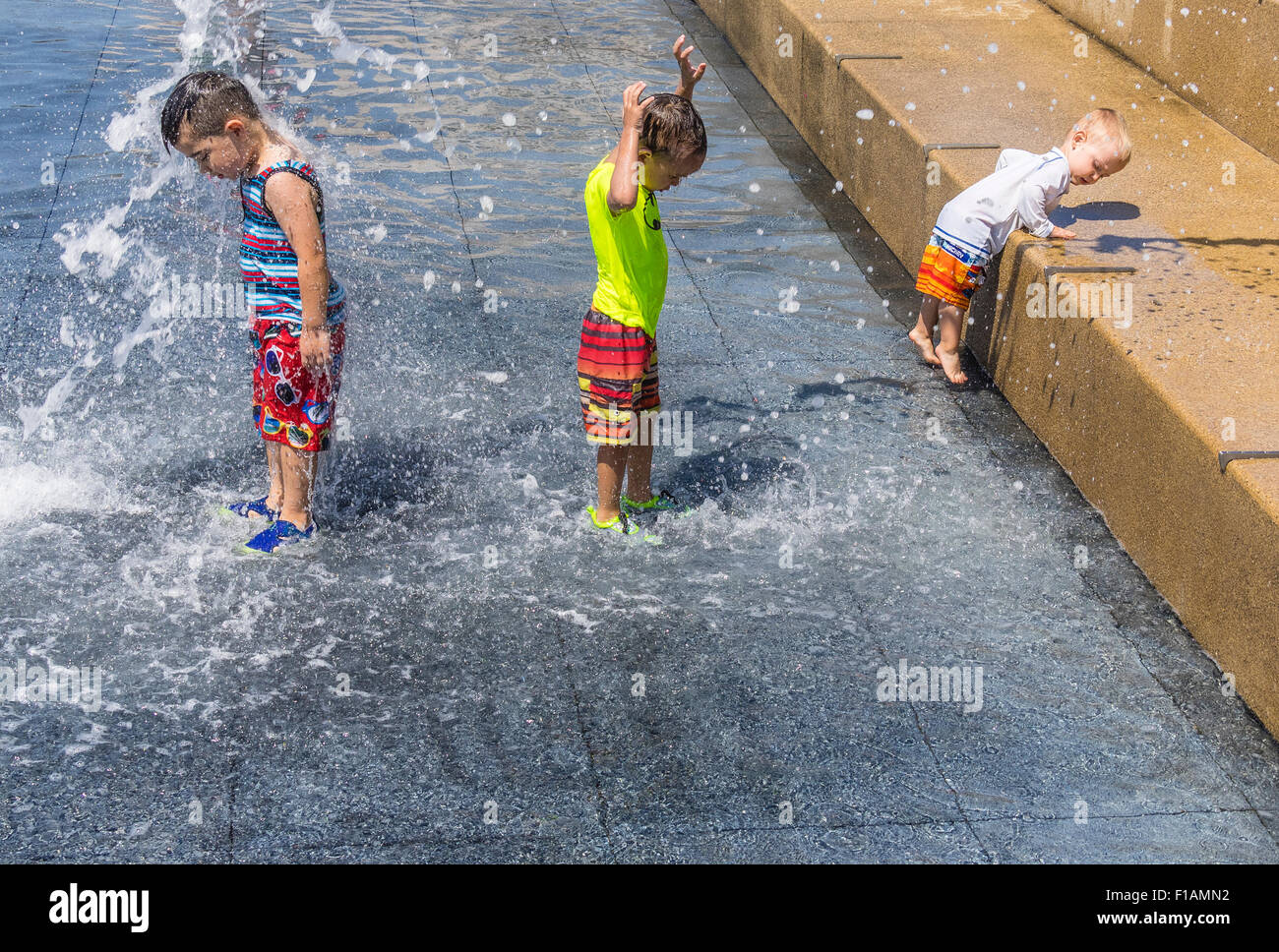 Children playing in water fountains while families look on at ...