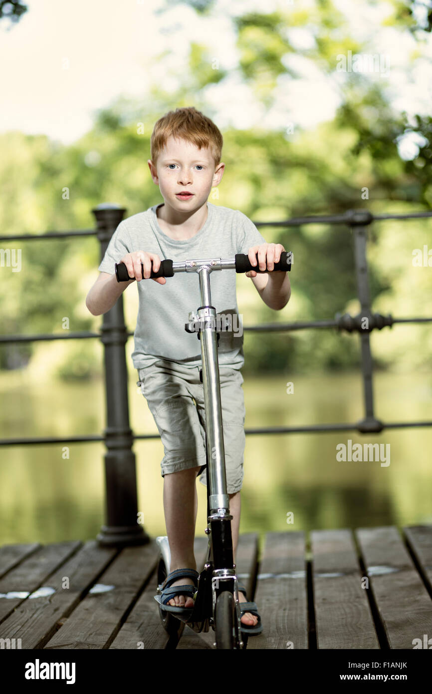 Portrait of little boy with push scooter standing on footbridge in a ...