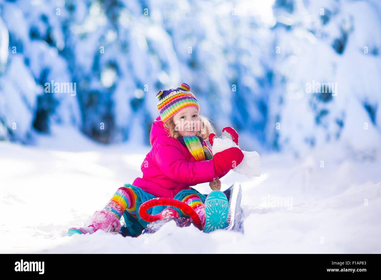 Little girl enjoying a sleigh ride. Child sledding. Toddler kid riding a sledge. Children play ...