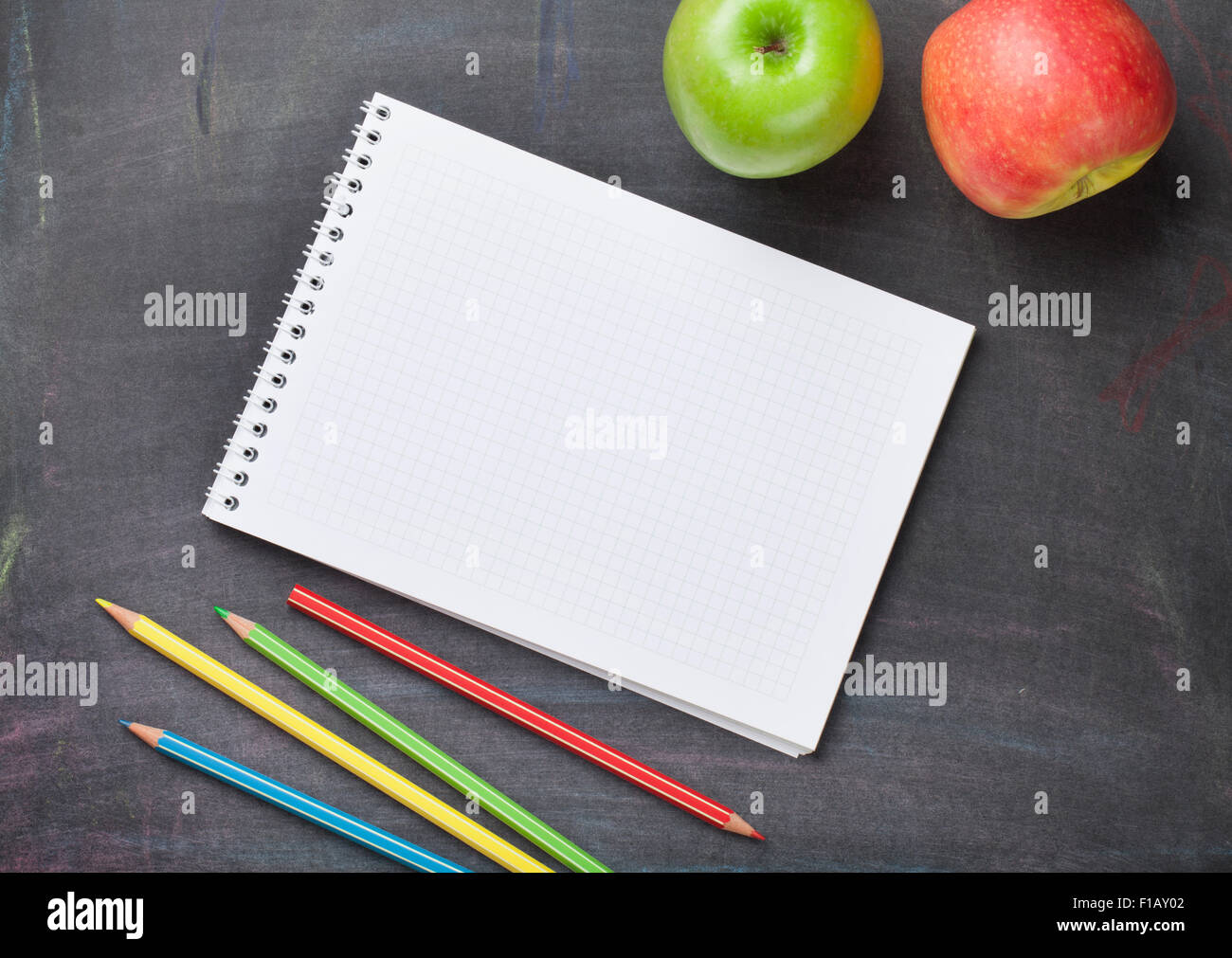 Blank notepad, colorful pencils and apples on blackboard background ...