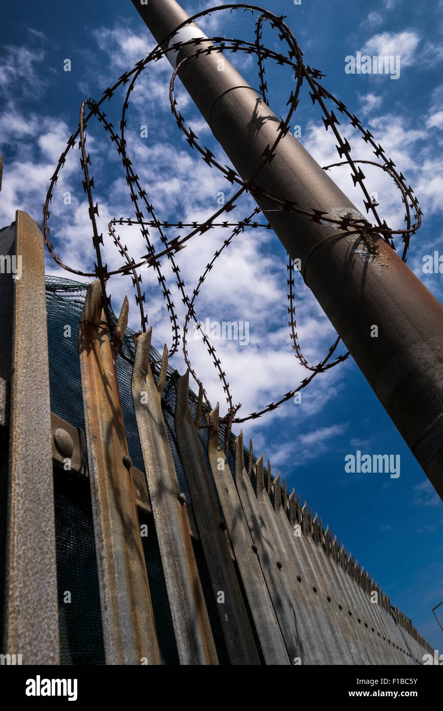 Barbed razor wire wrapped around a lampost by a spiked fence to keep ...