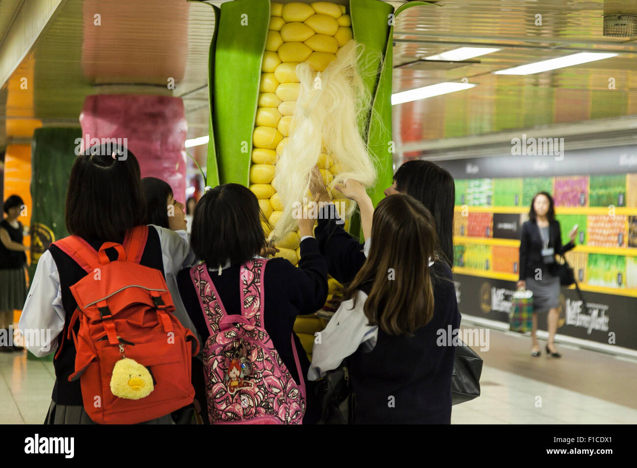 School girls touch a column displaying a giant corn in the Tokyo Metro ...