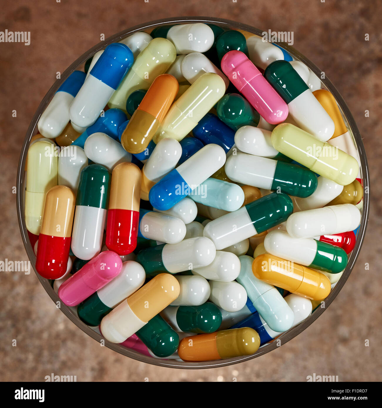 Medicinal capsules of many colors photographed from above in a glass ...