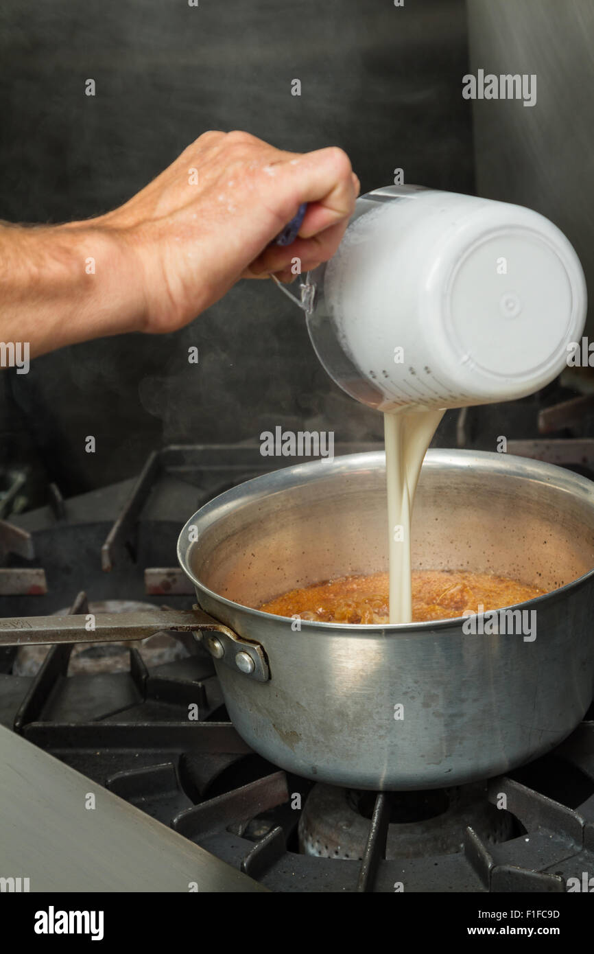 close up of a hand pouring milk into a pot with the ingredients to make ...