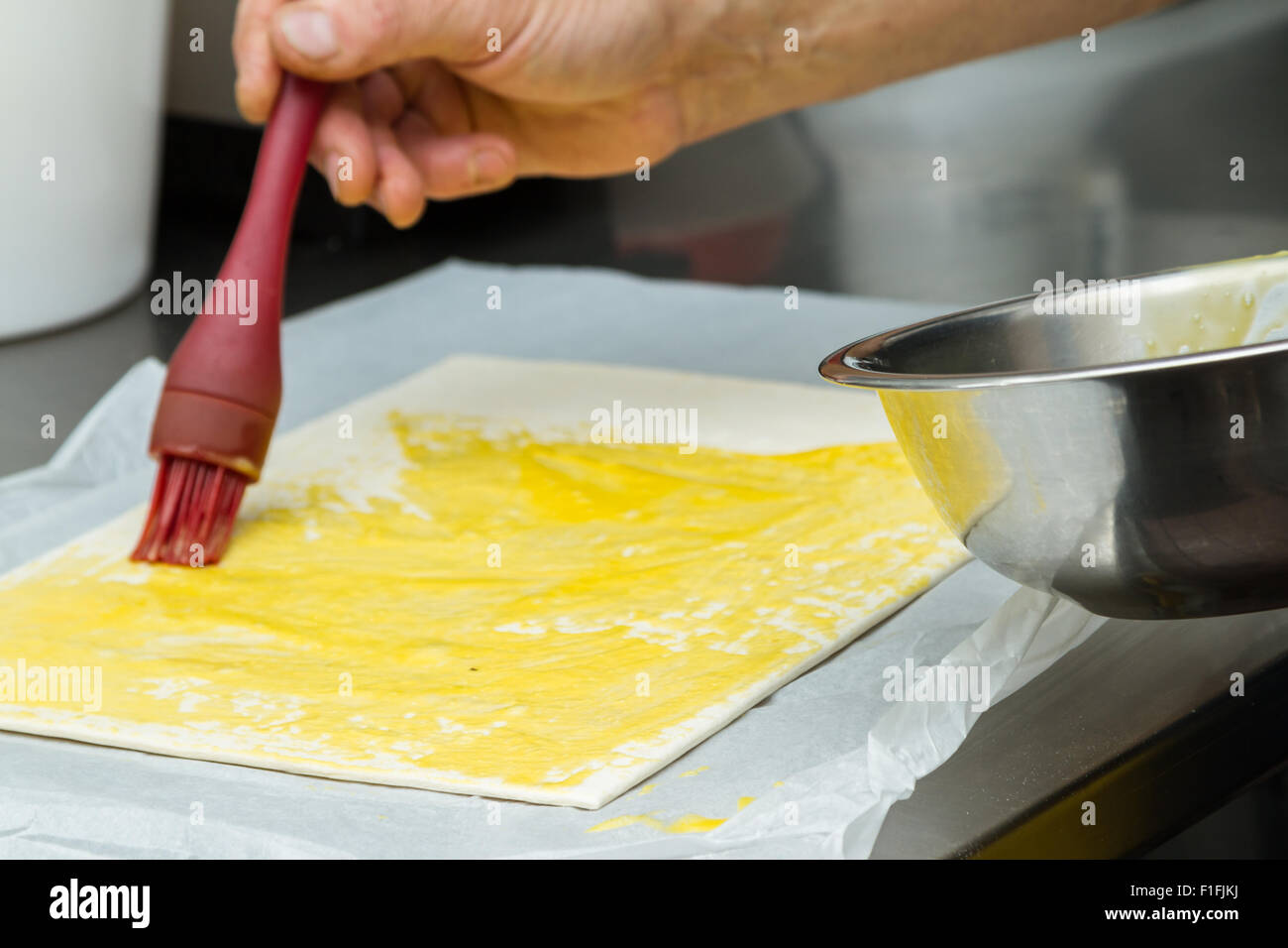 close up of a food grade brush spreading an egg mixture over a thin ...