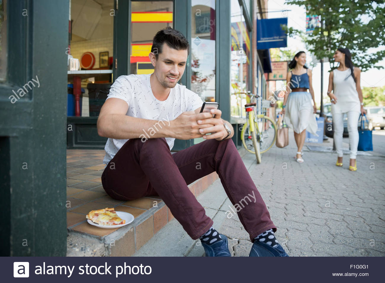 Man with pizza slice texting with cell phone storefront Stock Photo - Alamy