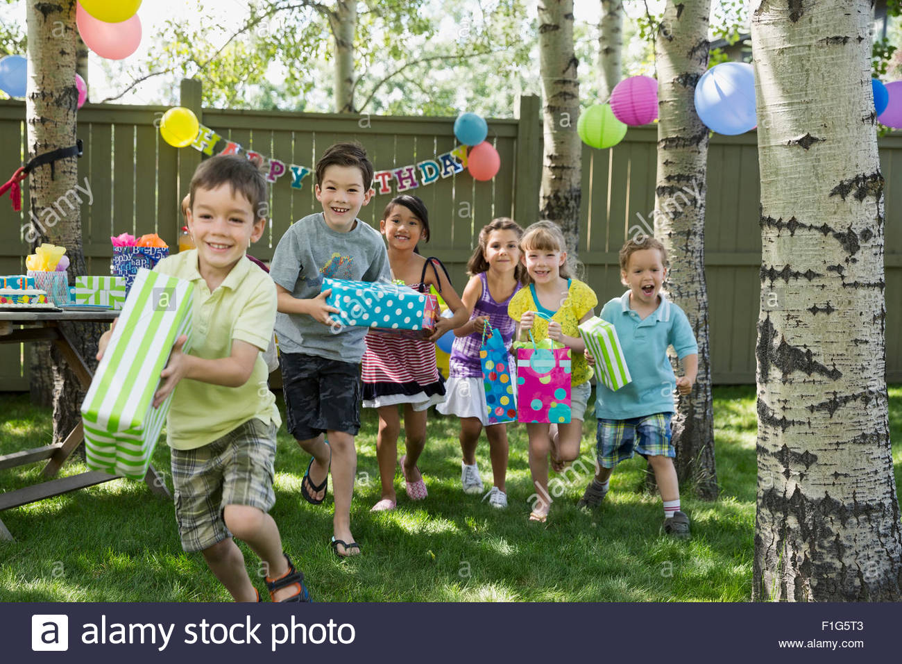Kids running with birthday gifts in backyard Stock Photo - Alamy