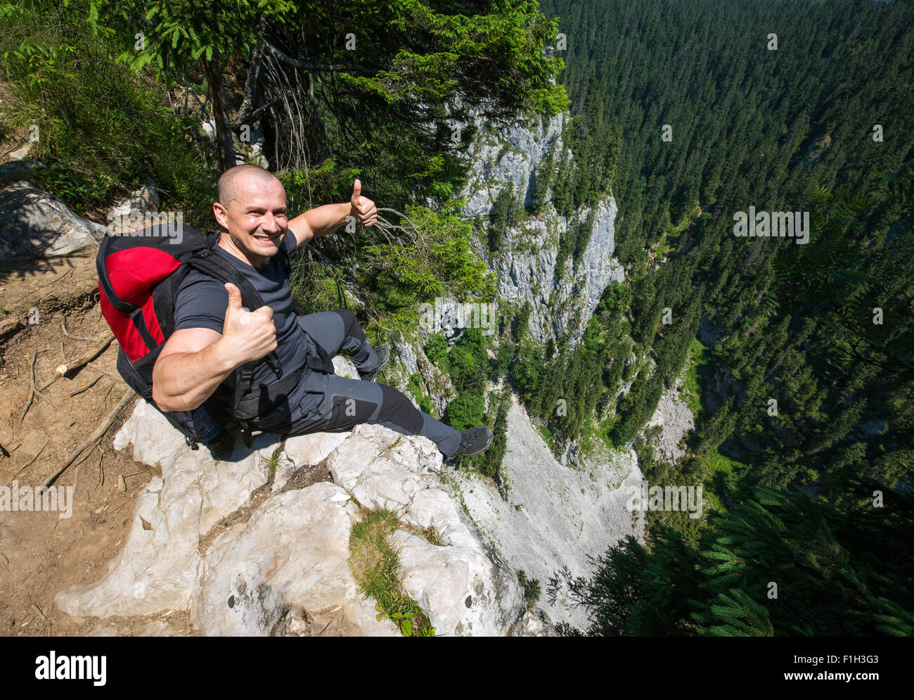 Happy man with thumbs up sitting on the edge of a very high cliff Stock ...