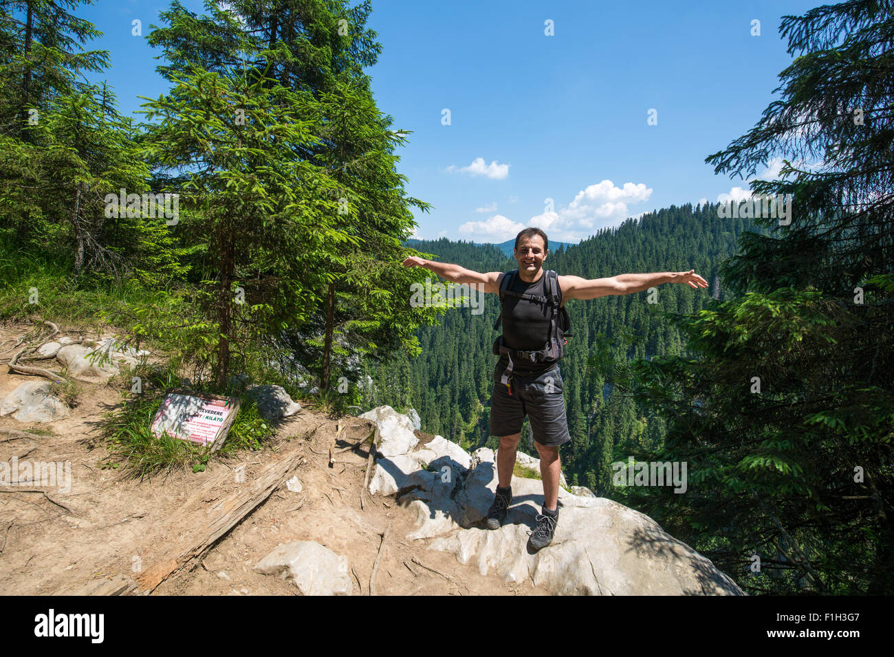 Happy man with arms raised standing on the edge of a very high cliff ...
