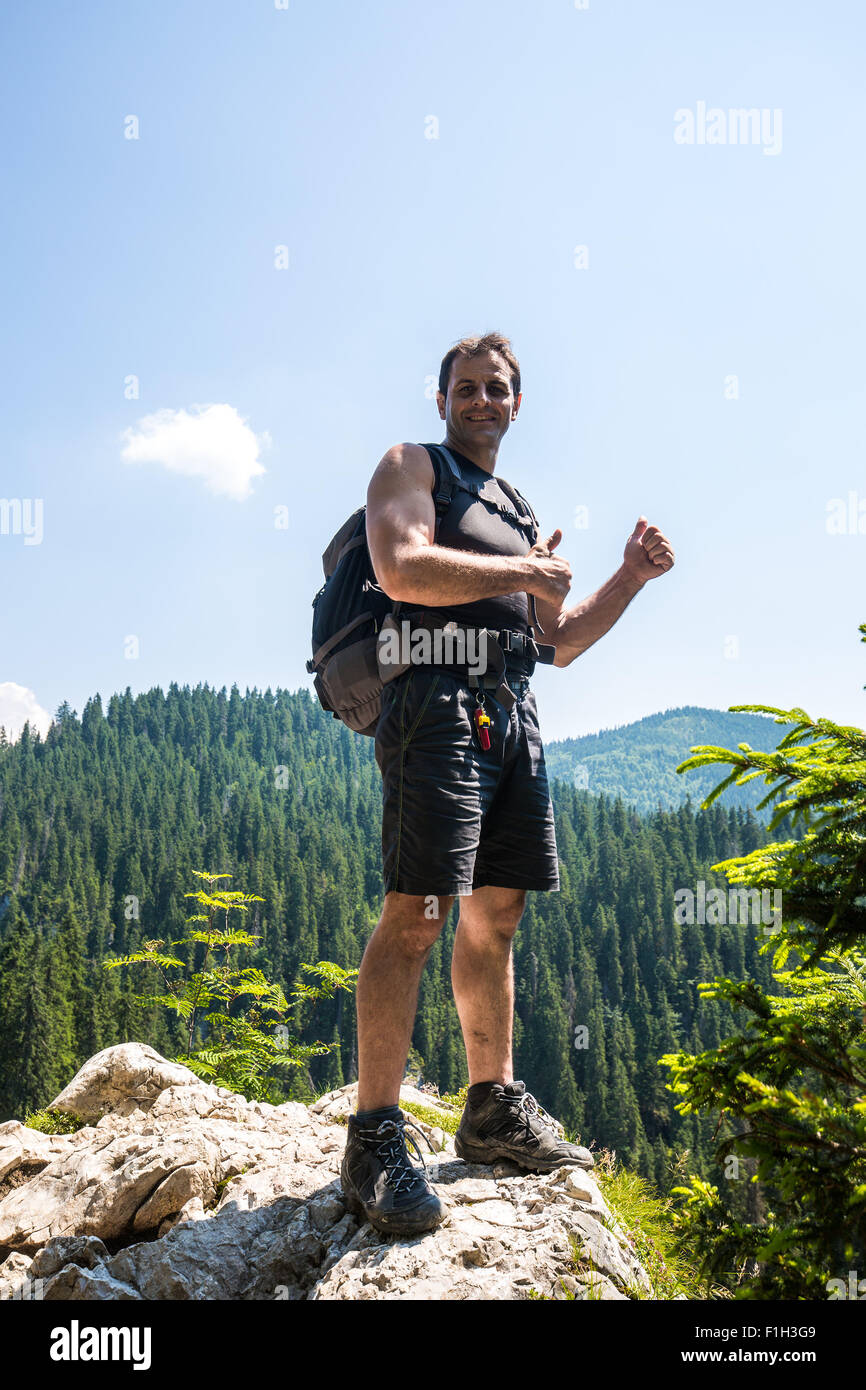 Happy man with thumbs up standing on the edge of a very high cliff ...