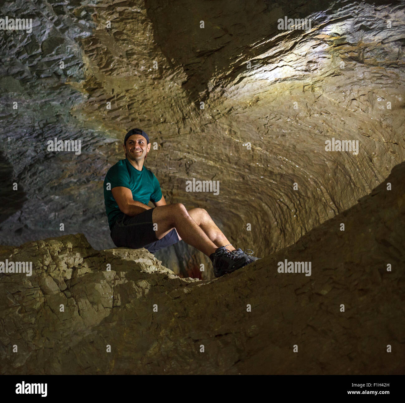 Happy man sitting on a large rock in a cave Stock Photo - Alamy