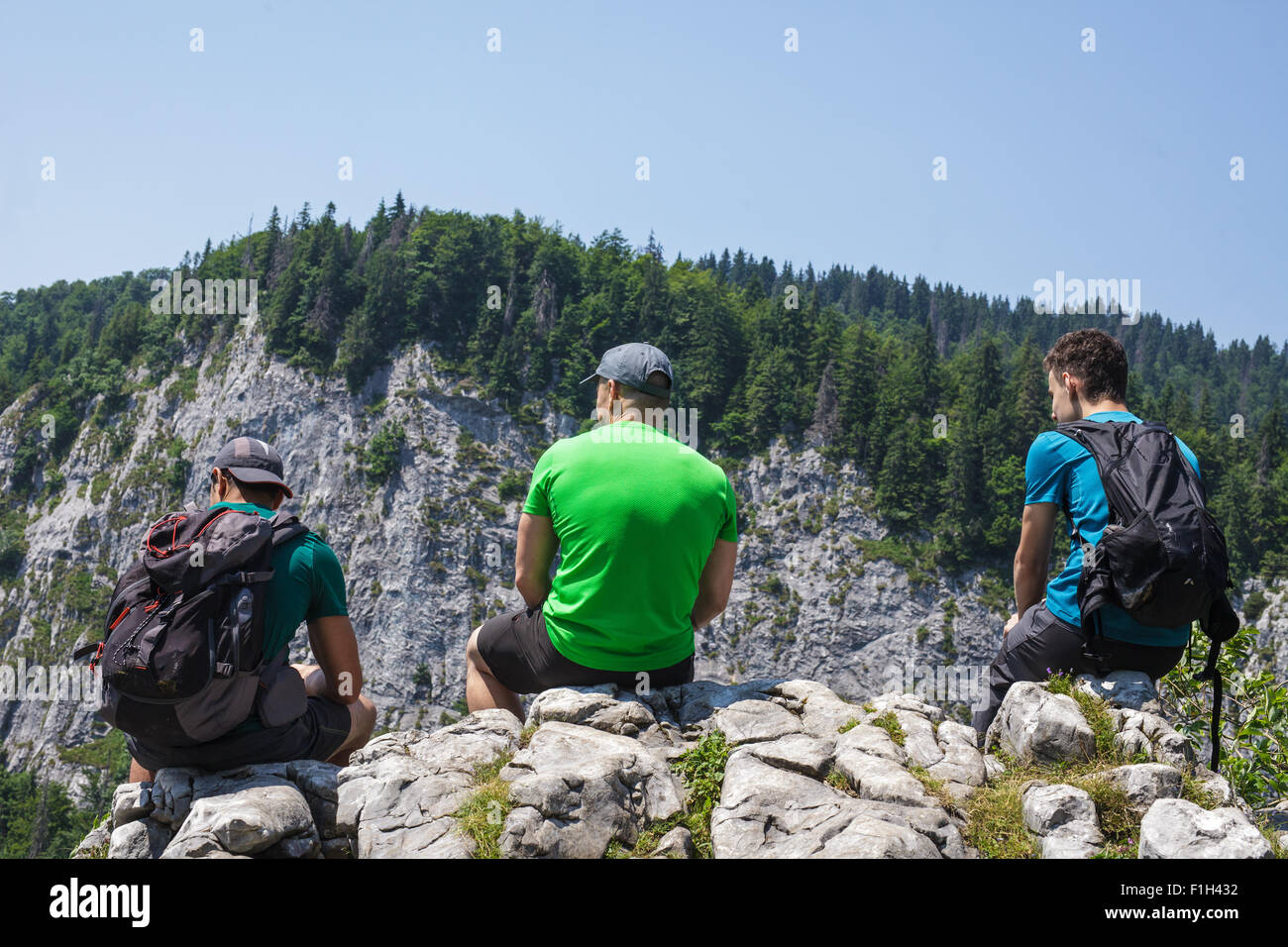 Happy male hikers sitting on the edge of a very high cliff Stock Photo ...