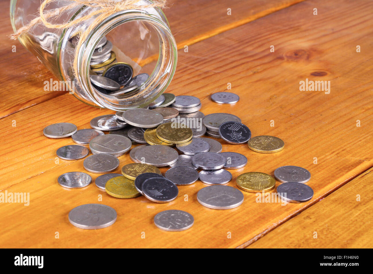 coins scattered outside the glass jar on the table with close-up ...