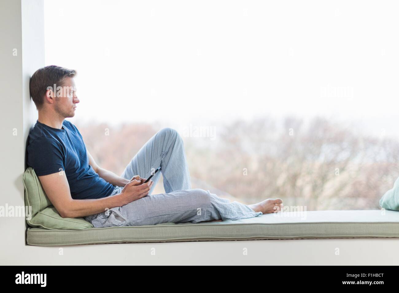 Mid adult man sitting on window seat, looking out of window Stock Photo ...