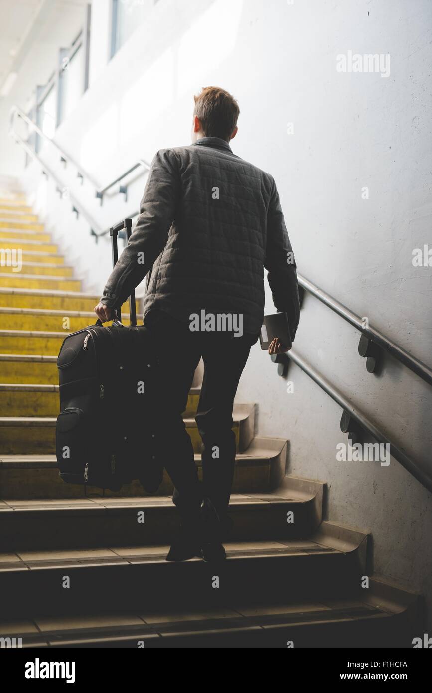Rear view of young businessman commuter on stairs carrying suitcase ...