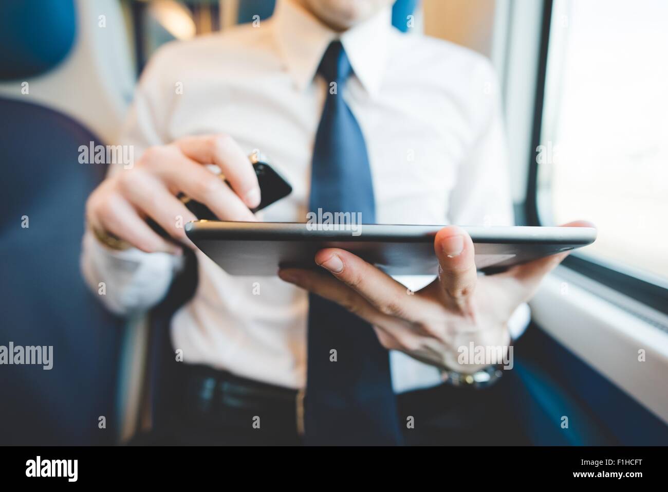 Portrait of young businessman commuter using digital tablet on train ...