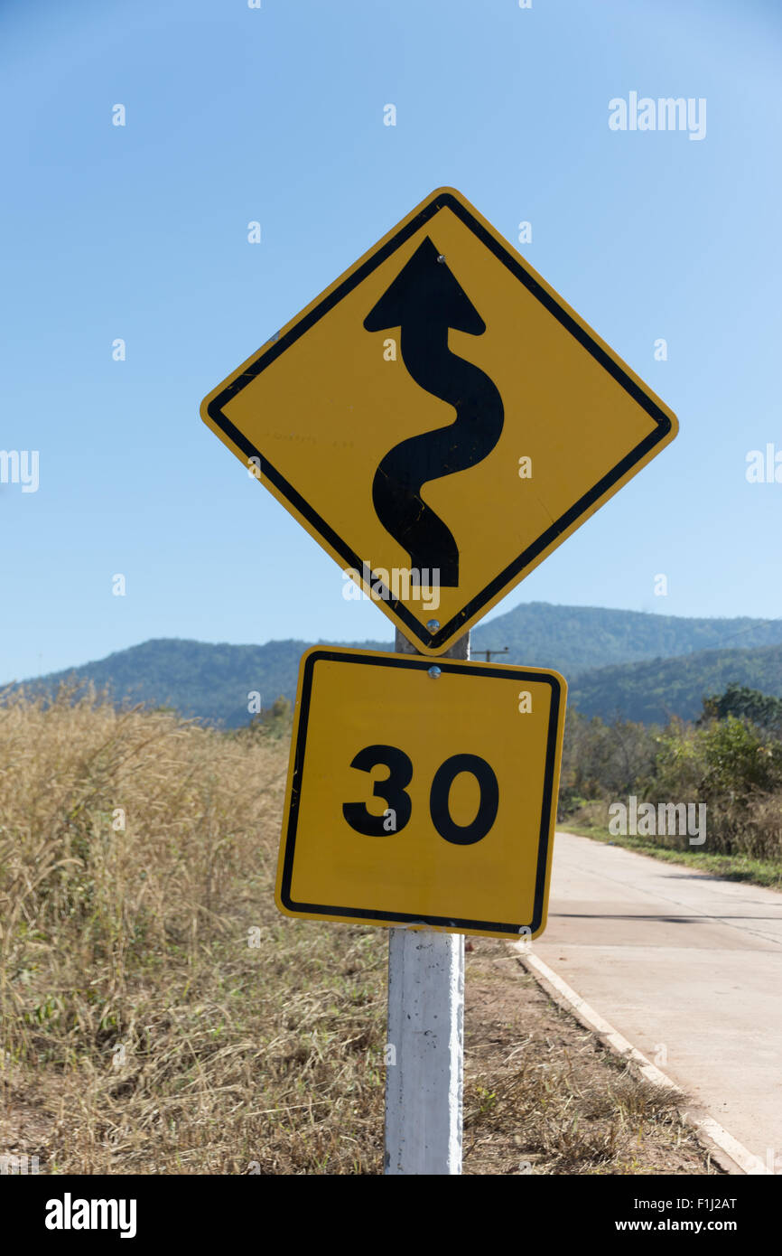 A Traffic sign warns of sharp turns ahead and speed limit on a road ...