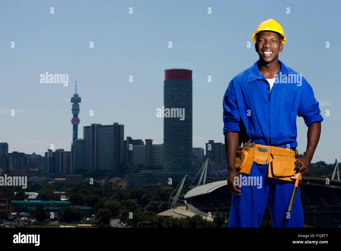 Construction worker wearing utility belt stands in front of cityscape ...