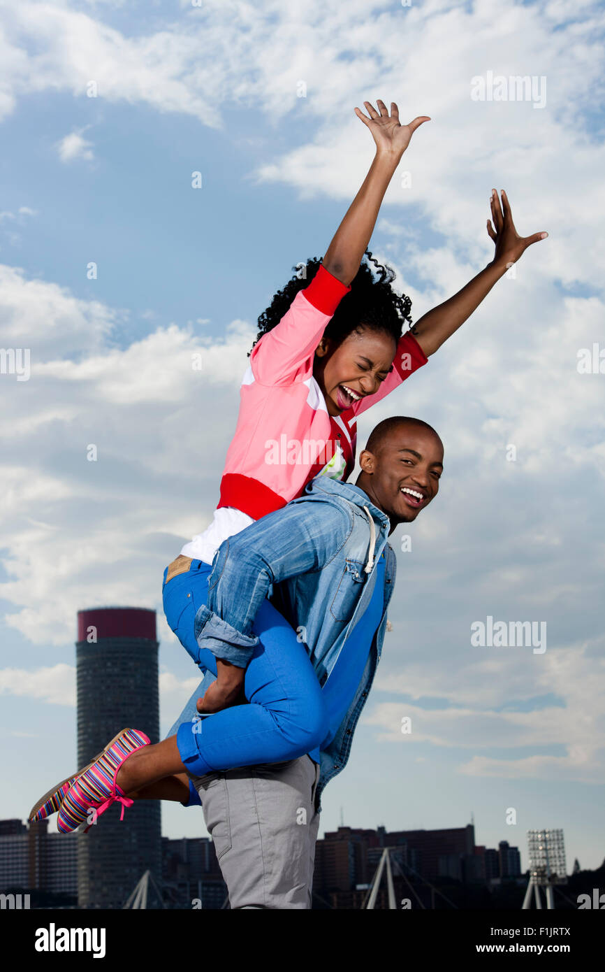 Young black woman sitting on man's shoulders in front of cityscape ...