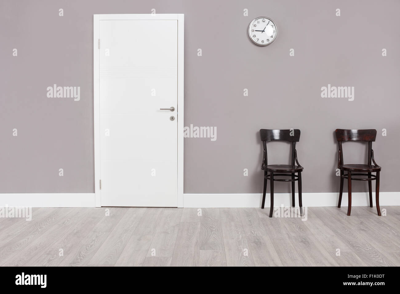 Two wooden chairs in a waiting room with a clock hanging on the wall ...