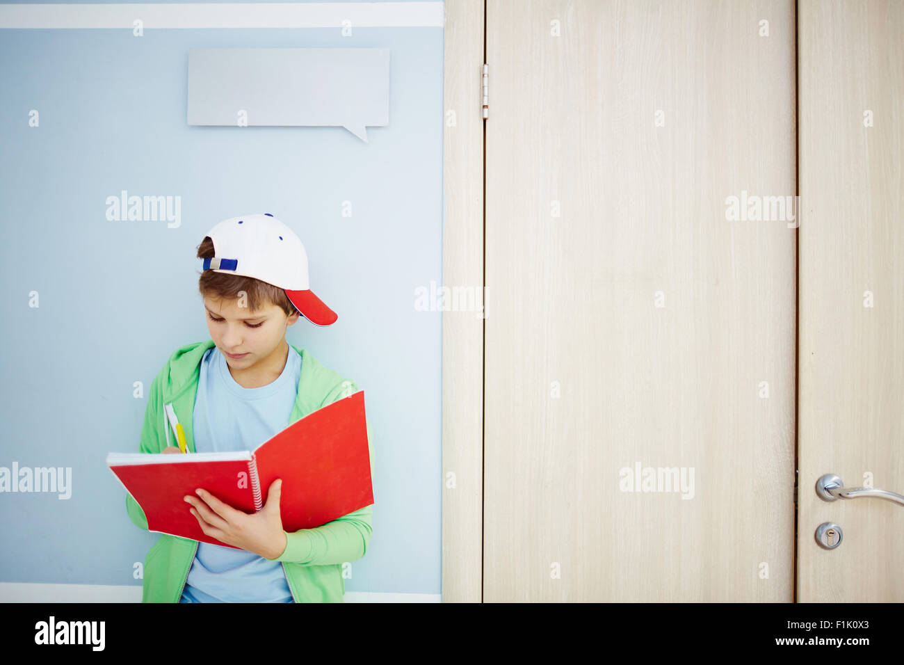 Clever boy making notes in exercise-book near classroom door Stock ...
