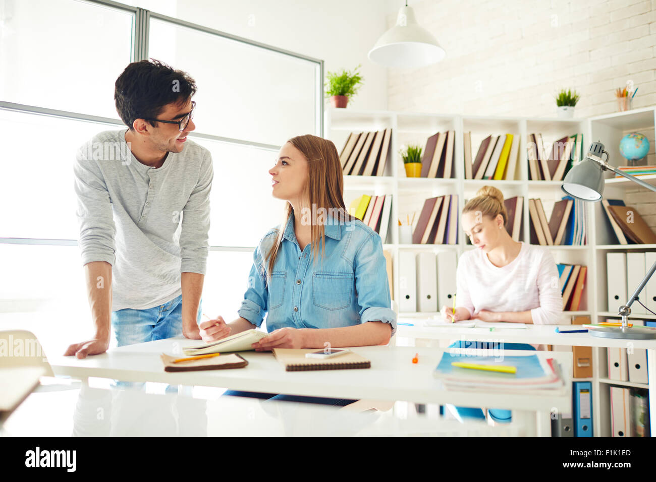Young girl sitting by desk and carrying out assignment while talking to ...