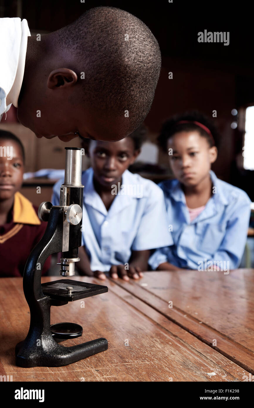 African male student looks into a microscope while the other students ...