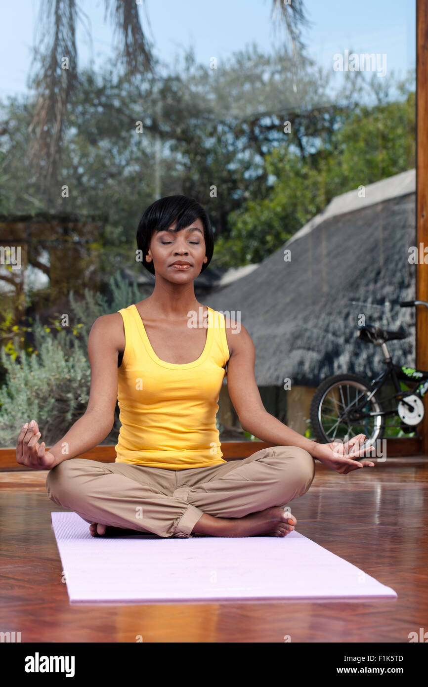 Young African woman meditating alone in her lounge Stock Photo - Alamy