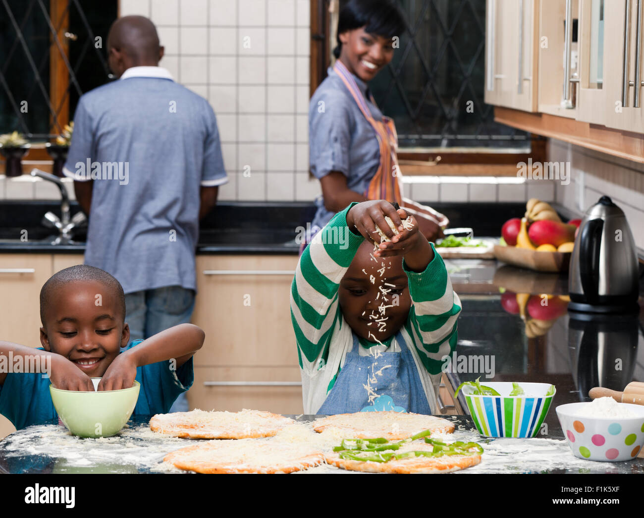 Two young African children preparing food together while their parents ...